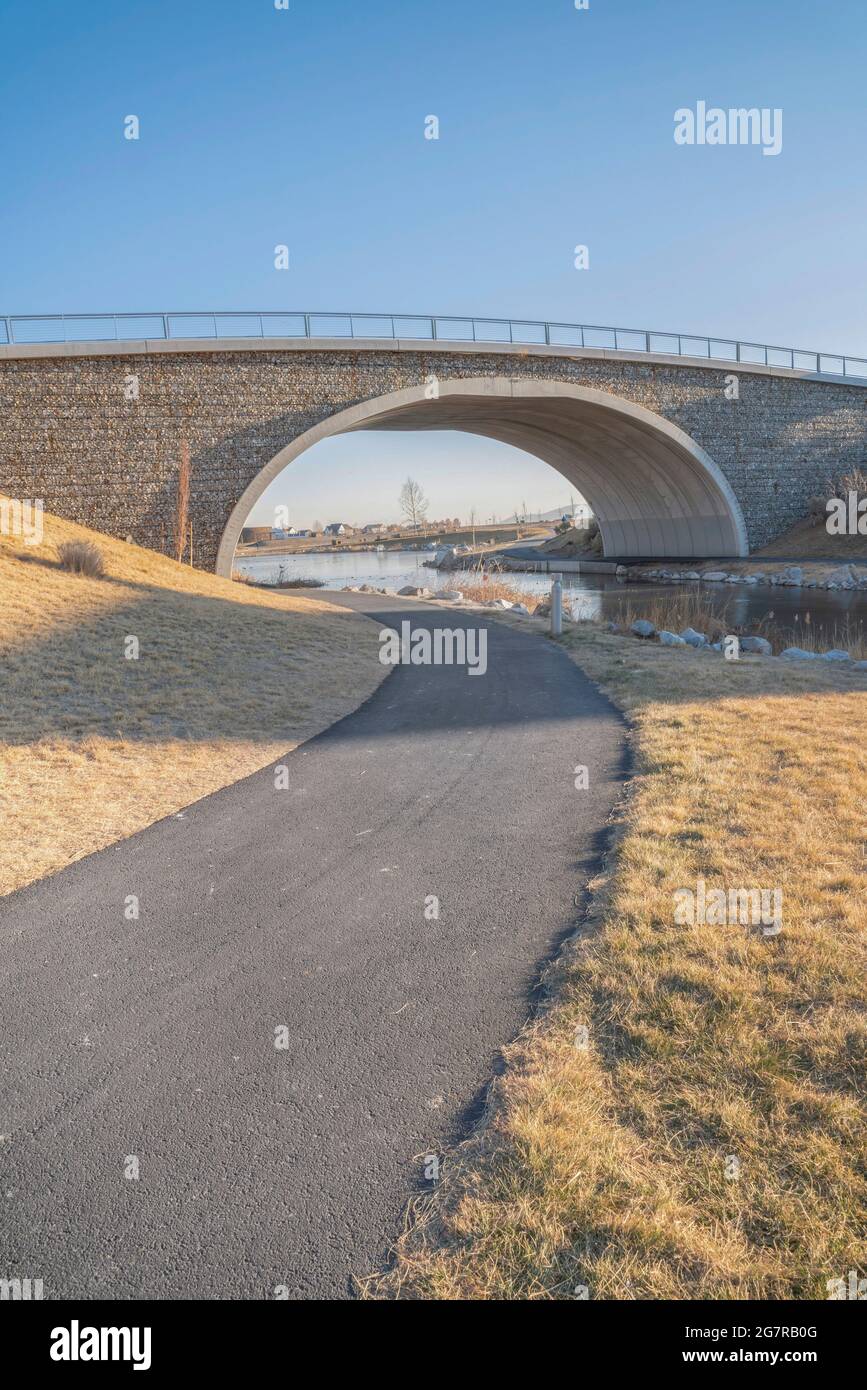 Concrete trail in the middle of a grass with a view of an arched bridge ...