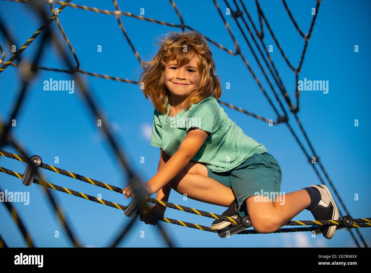 Cute smiling kid climbing the net at the playground. Kids rope park ...