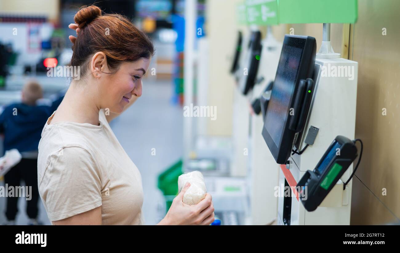 Caucasian woman uses a self-checkout counter. Self-purchase of ...