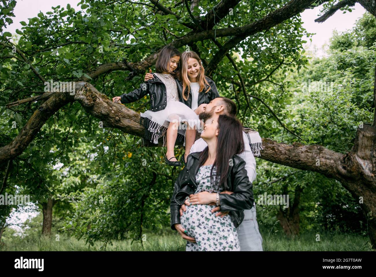 Handsome husband embracing his pregnant wife while their two daughters ...