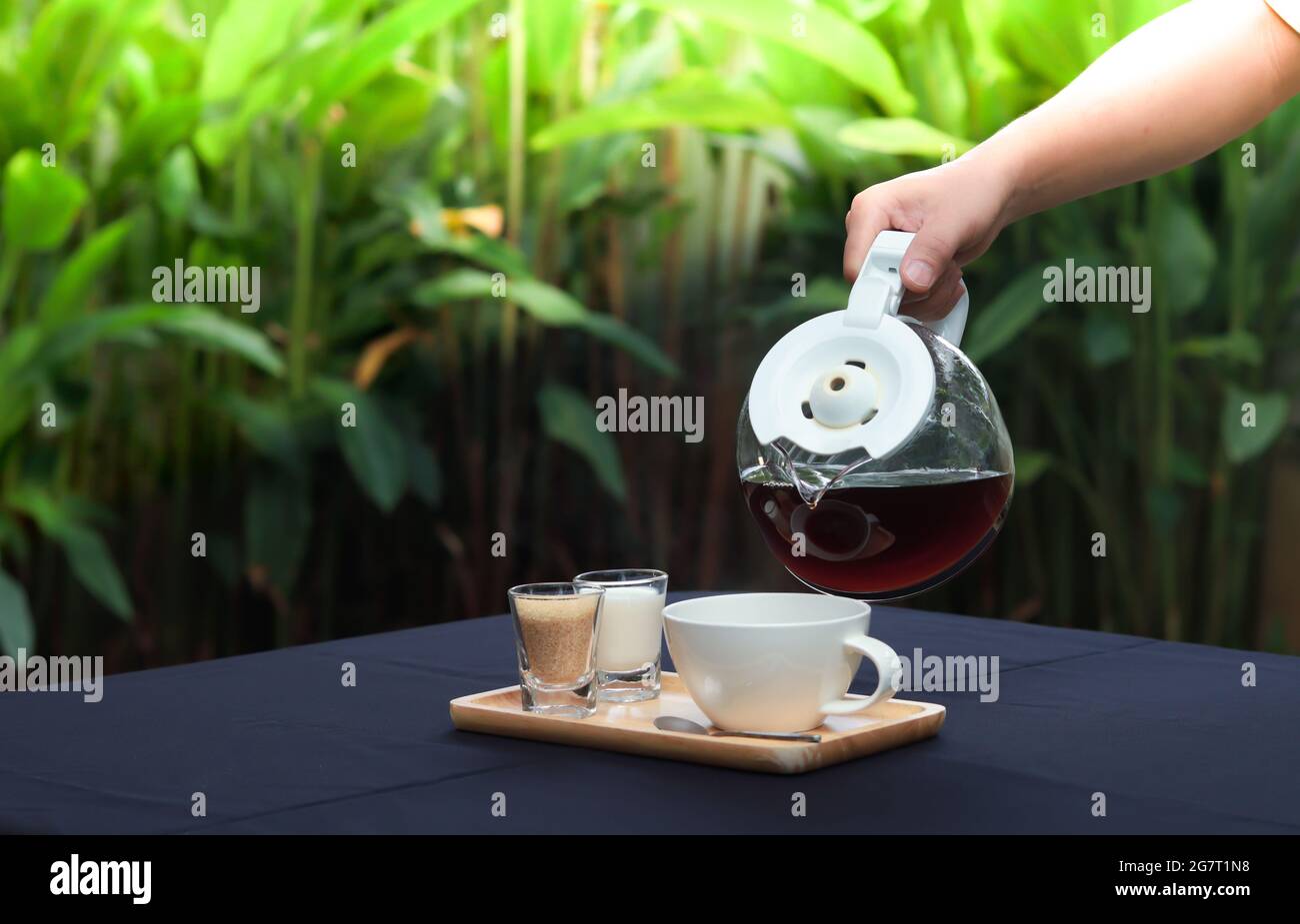 Hand holding a pot of coffee, pouring in a glass on a table with a ...