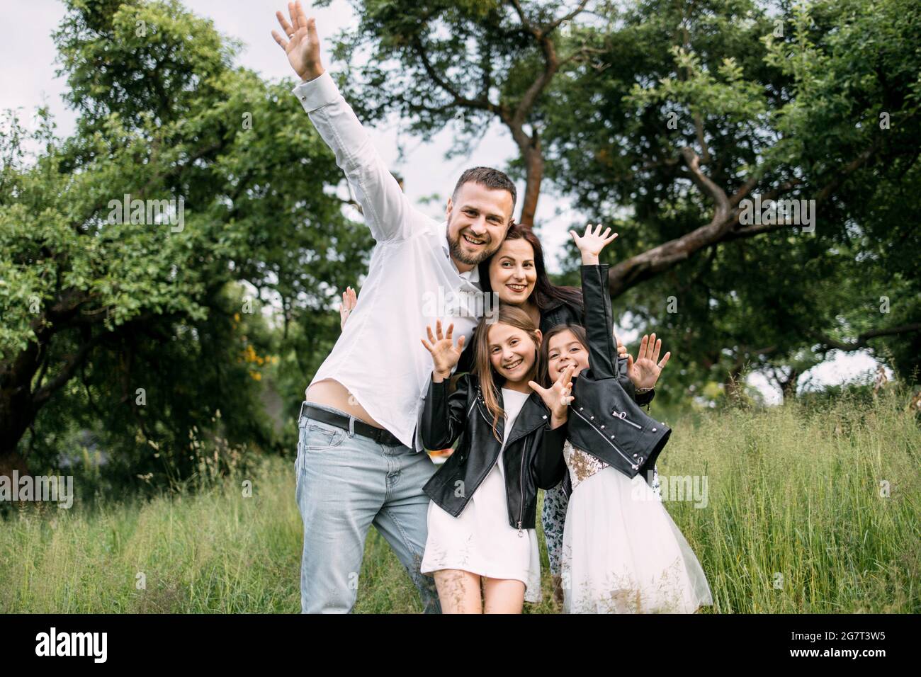 Positive parents and their two cute daughters smiling and waving on ...