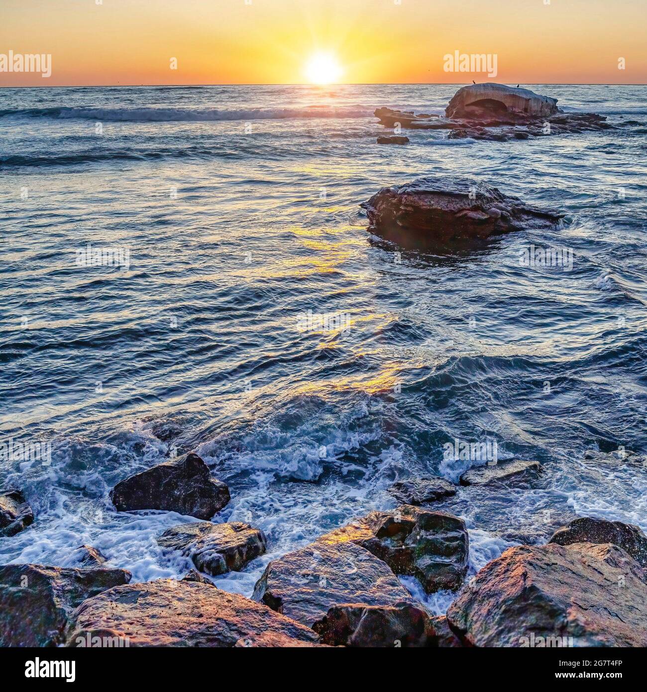 Square frame Golden sunset by the scenic ocean with huge gray rocks in ...