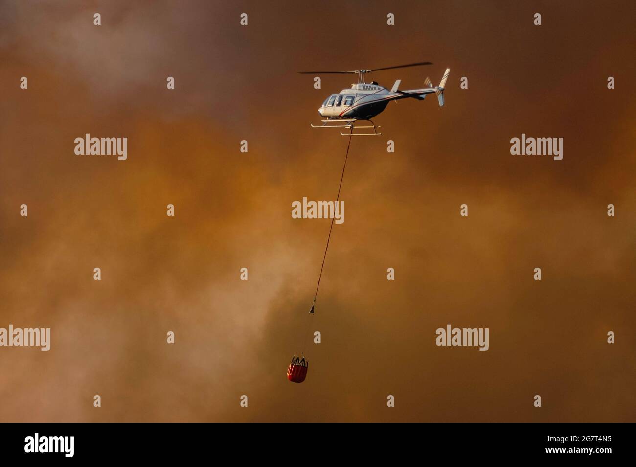 Fire fighting helicopter in smoke with water bucket Stock Photo - Alamy