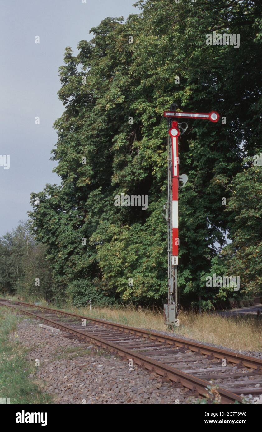Vertical shot of a red pole next to a thin long railroad with a bushy ...