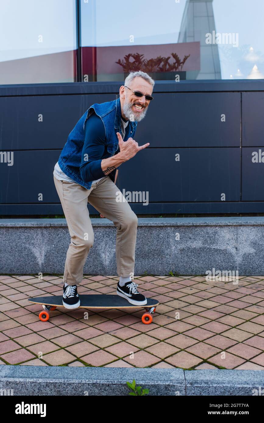 full length of happy man with open mouth riding longboard and showing ...