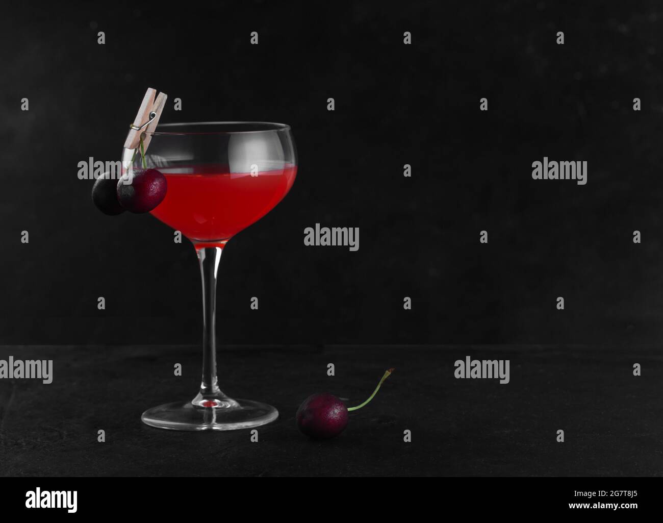 A glass with an alcoholic cocktail of red color decorated with cherries ...