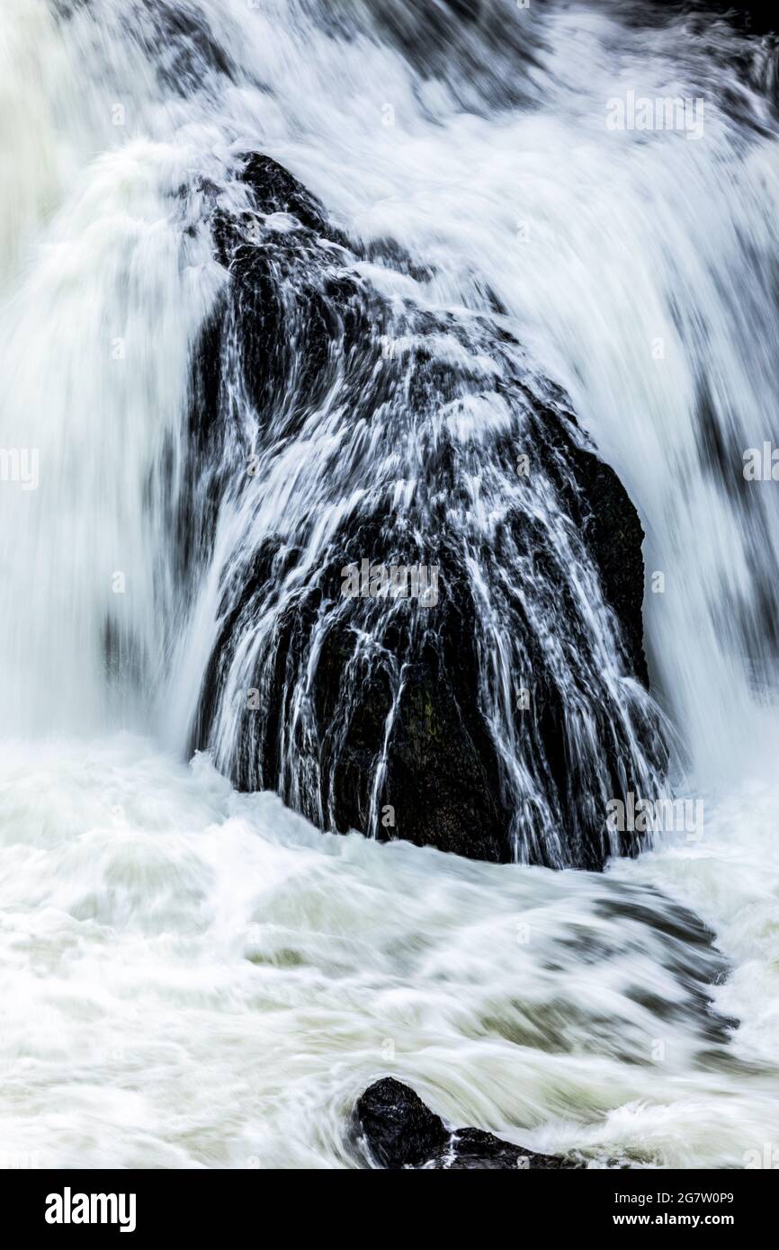Blurry motion of flowing water of waterfall over big black rock Stock ...
