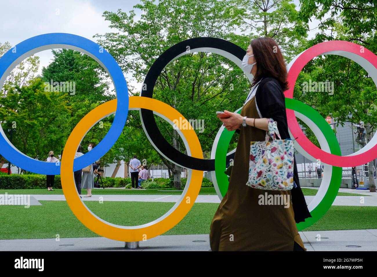 A woman wearing a face mask walks past Olympic Rings near the National ...