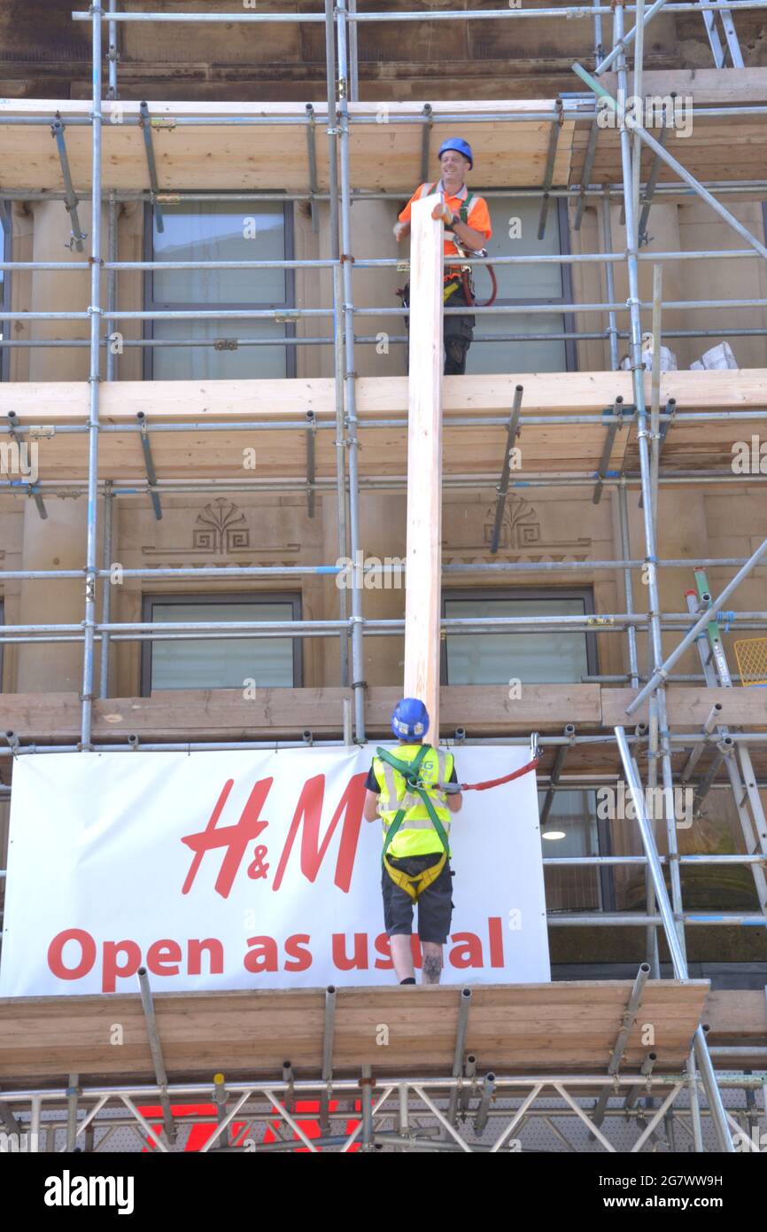 Builders pass a wooden plank upwards on a scaffolded building in ...