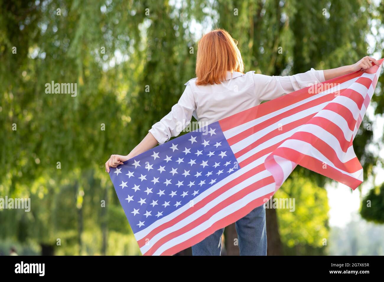 Rear view of happy young red haired woman posing with USA national flag ...