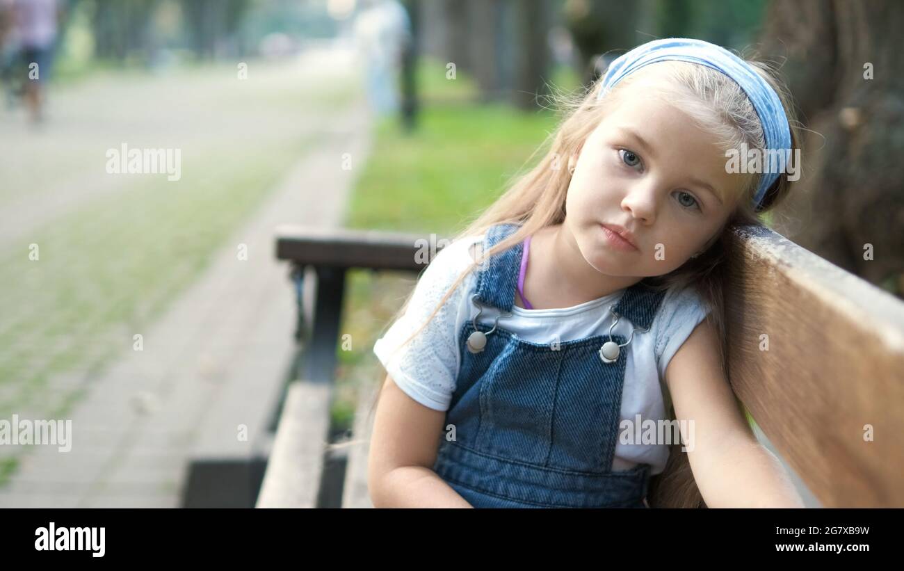Little serious child girl sitting alone on a bench in summer park Stock ...