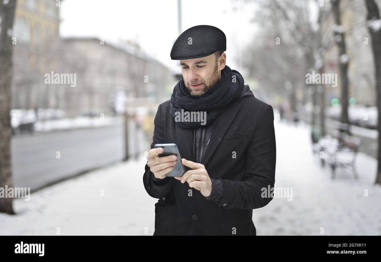 Caucasian man wearing a winter coat with a hat and using his phone ...