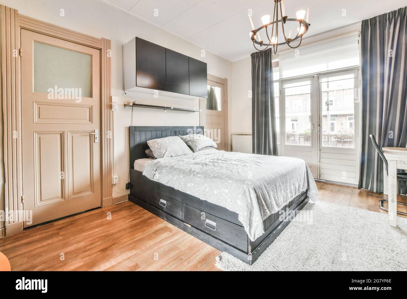 Bedroom with bed, laminate flooring and curtained windows Stock Photo ...