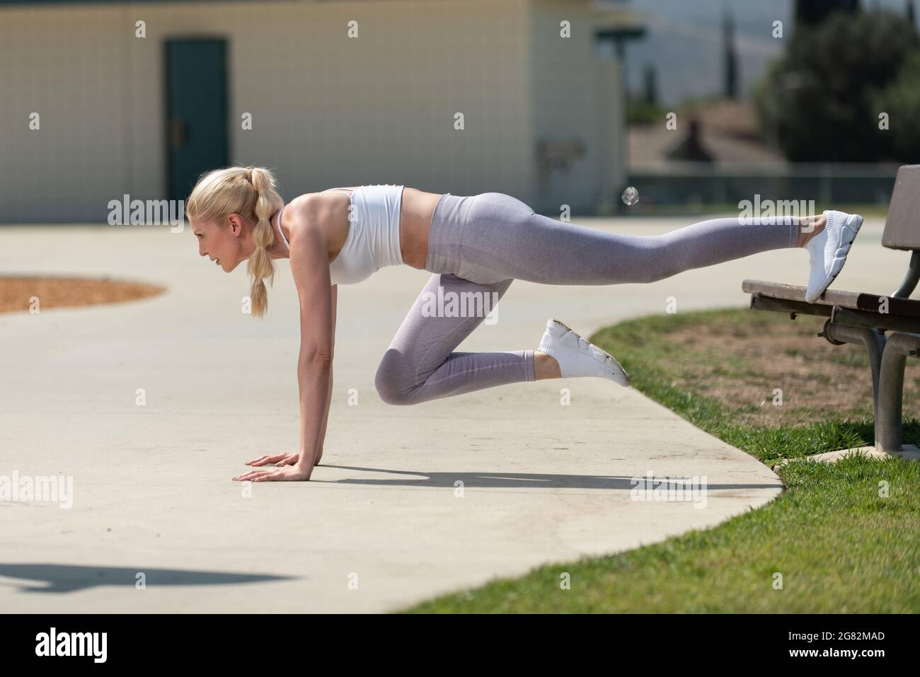 Healthy and fit atrractive blonde woman bridging on park sidewalk to ...
