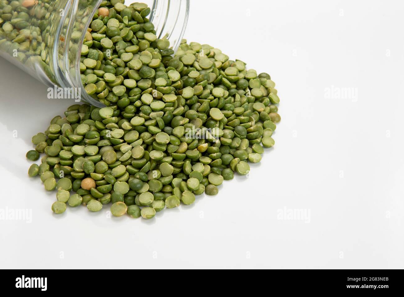 glass pot with dried peas in halves pouring out in a white background ...