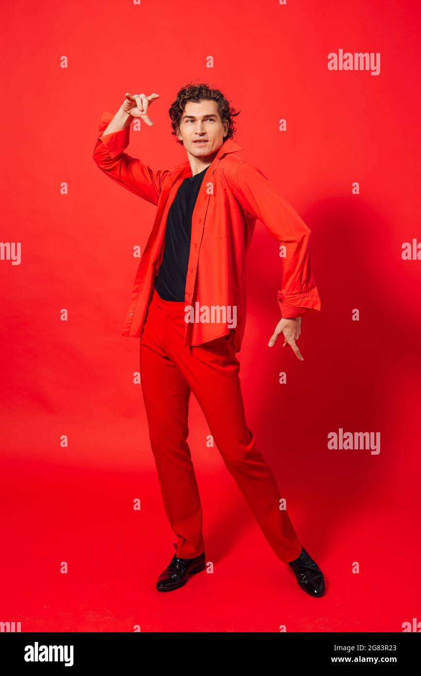 Portrait of a tall handsome man dressed in red shirt posing on the red ...