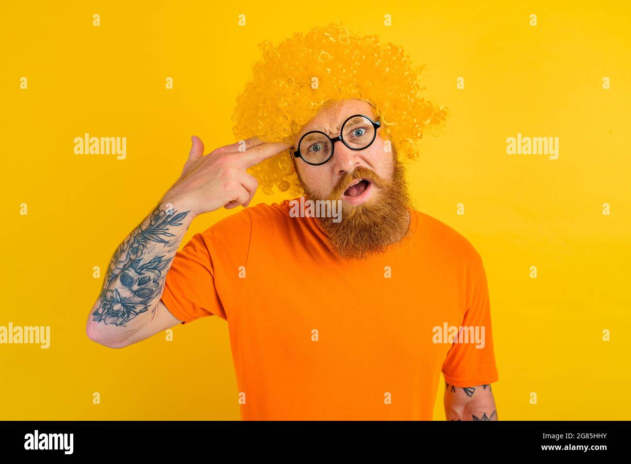 man with beard, yellow wig and glasses does a gun gesture with the hand ...