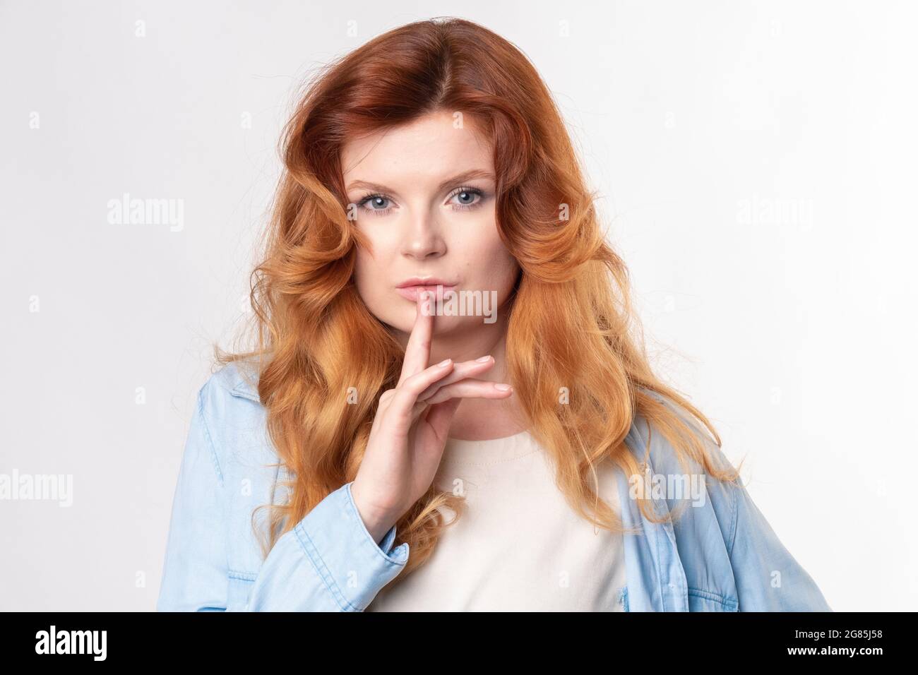 Portrait of young business woman keeping finger on her lips and asking ...