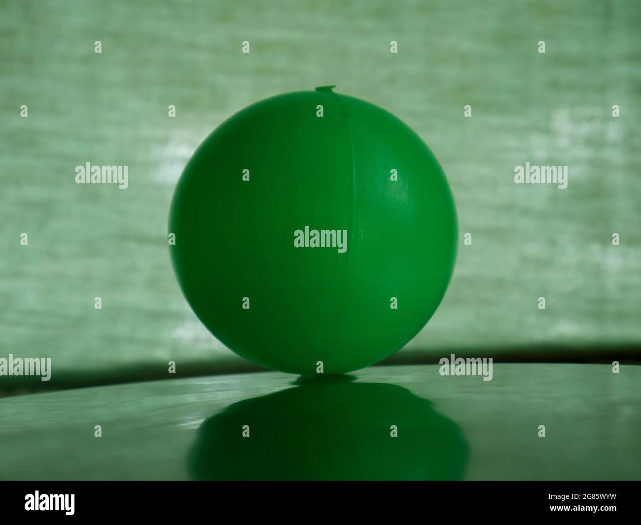 Green color plastic cricket ball kept on glass floor with reflection ...