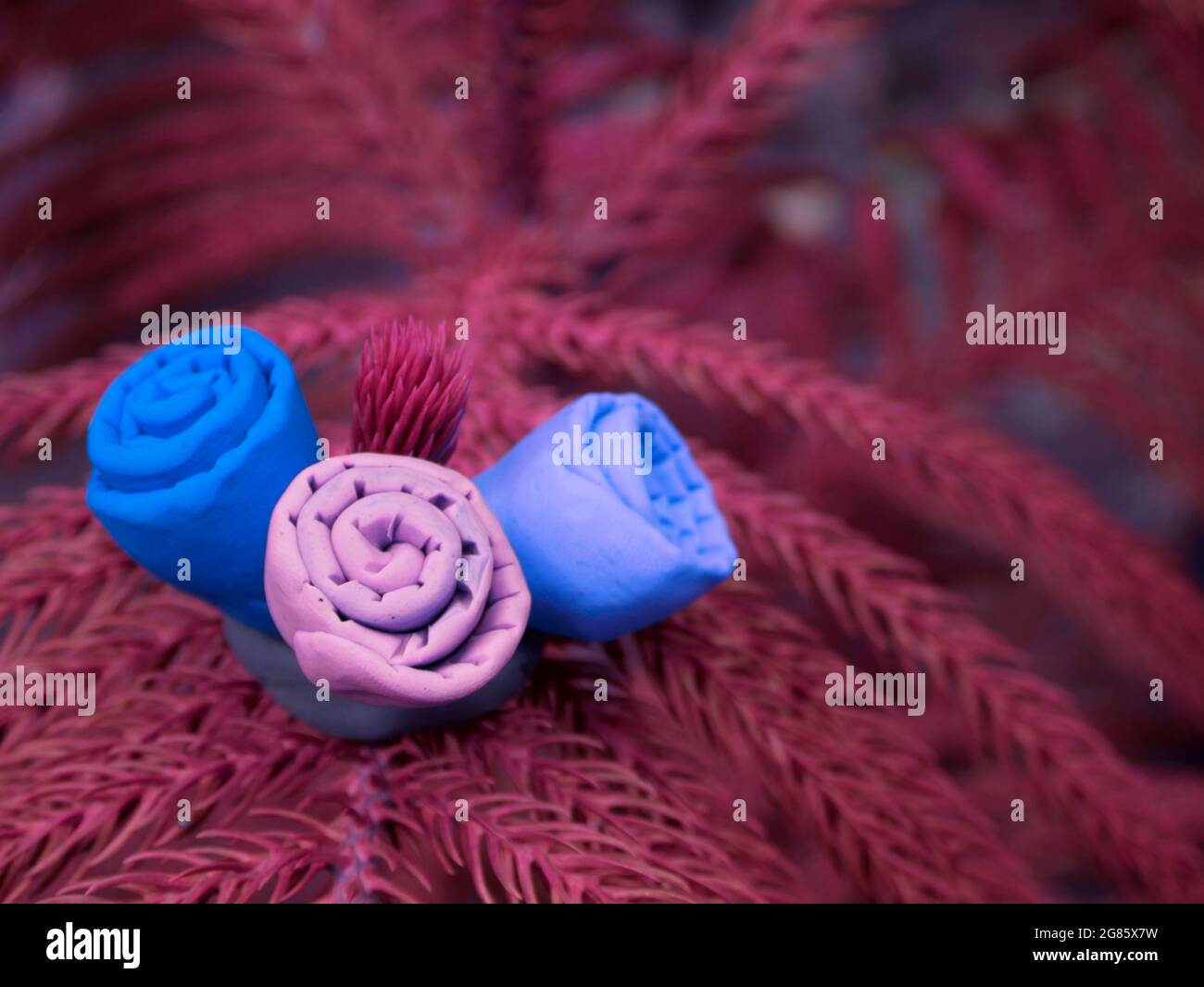 hand made three clay art blueish flower kept on thorn leaves surface at ...