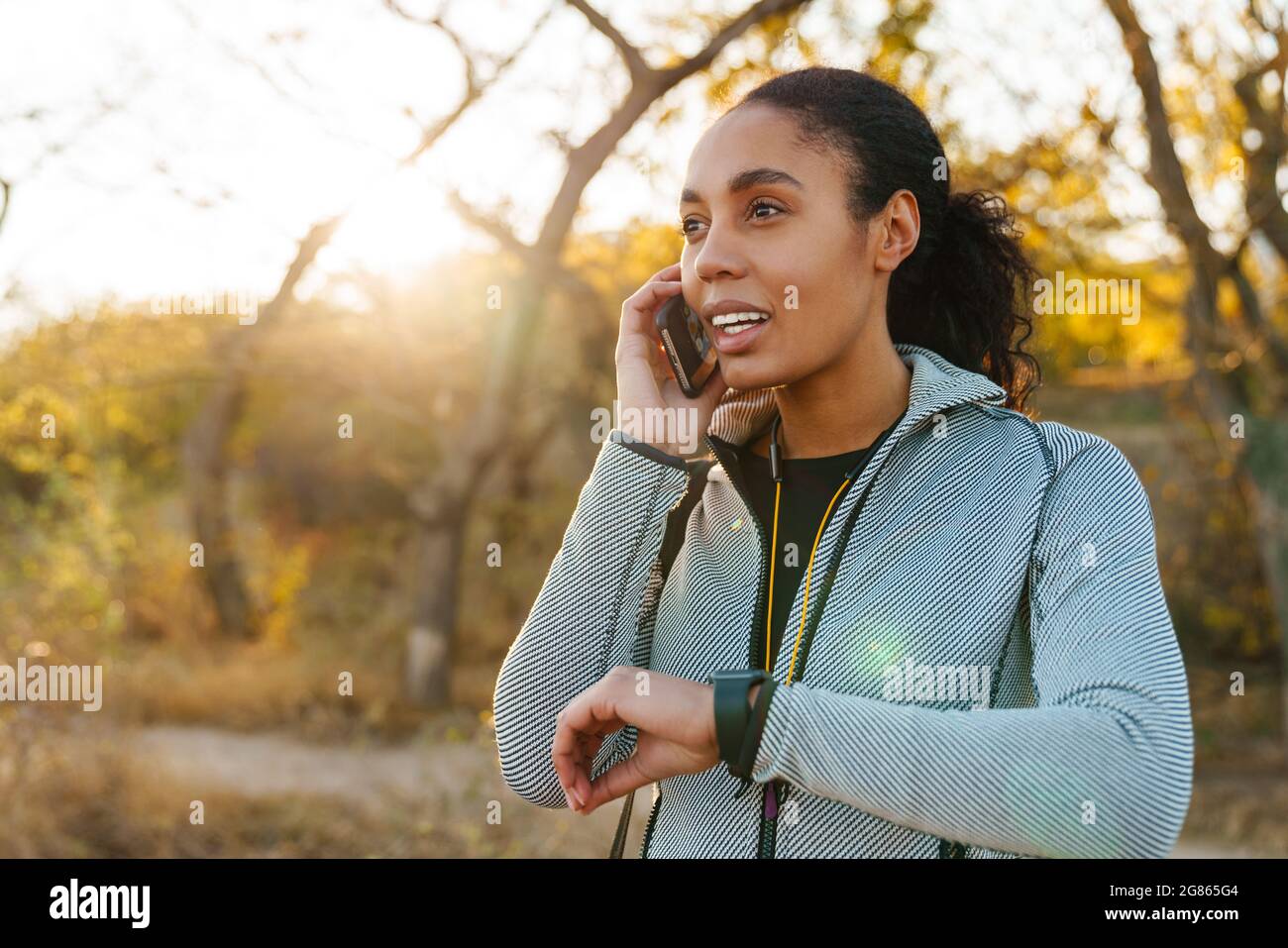 Pleased african american sportswoman talking on cellphone while using ...