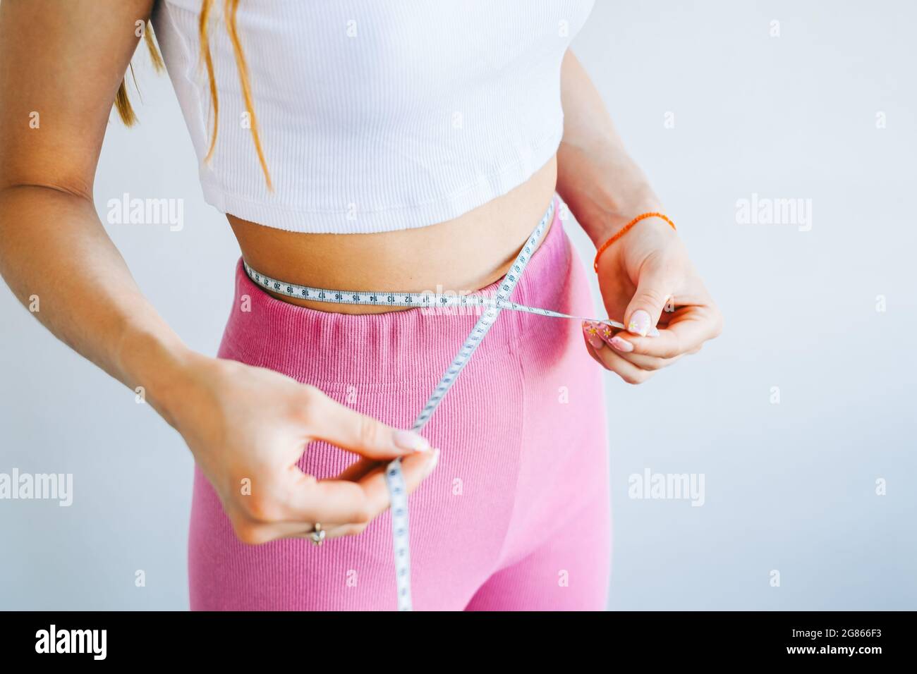 Slim woman measuring her waist's size with tape measure on white ...