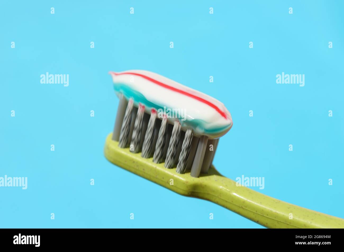 Green plastic toothbrush with striped toothpaste on blue background ...