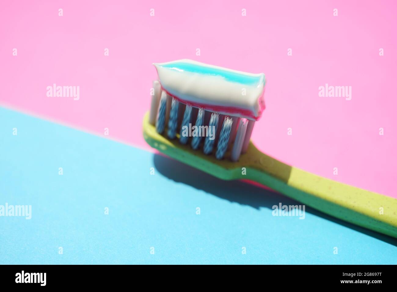 Green plastic toothbrush with striped toothpaste on a pink blue table ...