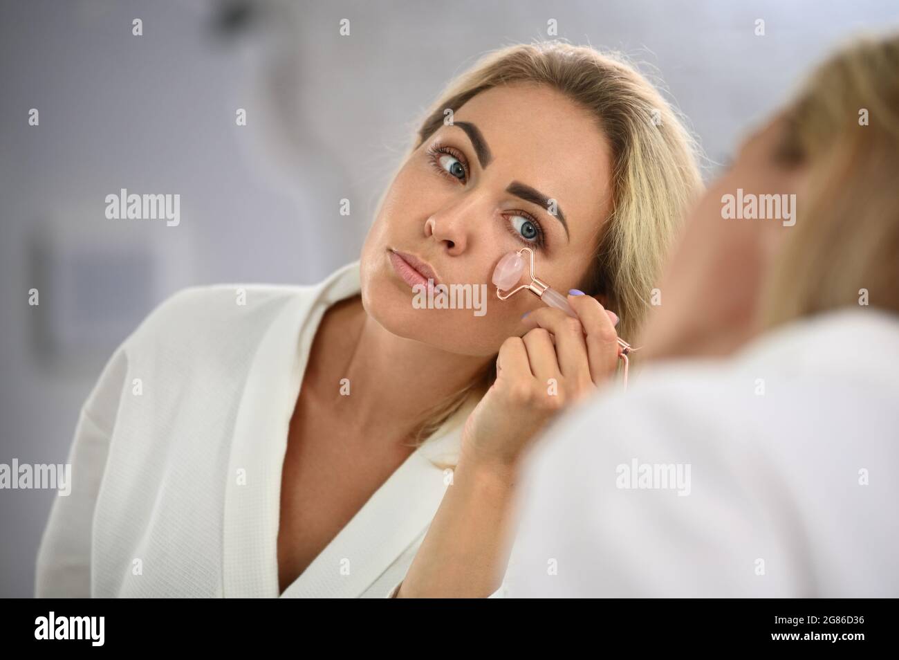 Reflection in the mirror of a beautiful woman massages her face with a ...