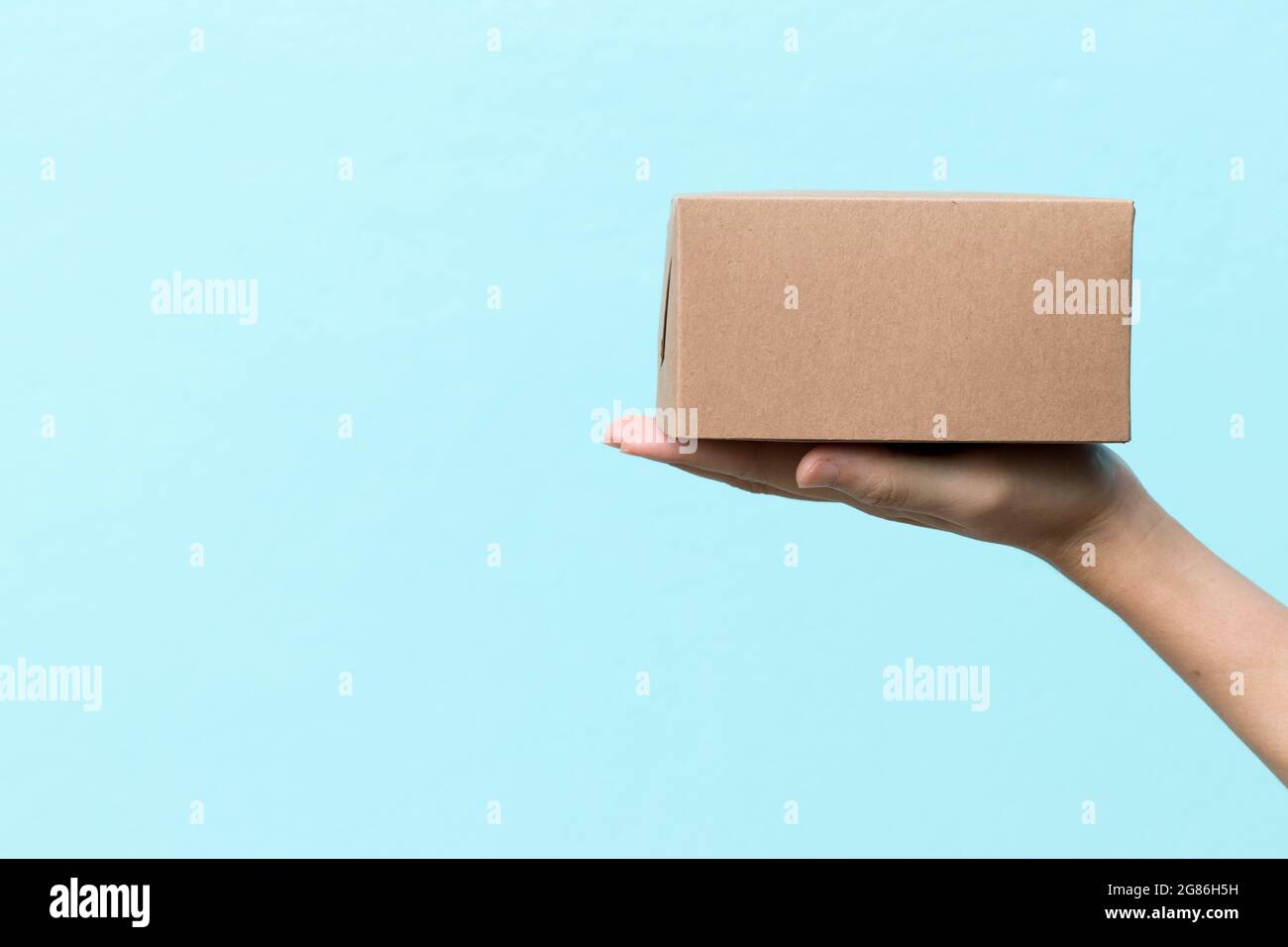Woman hand hold the brown corrugated box on blue wall background with ...