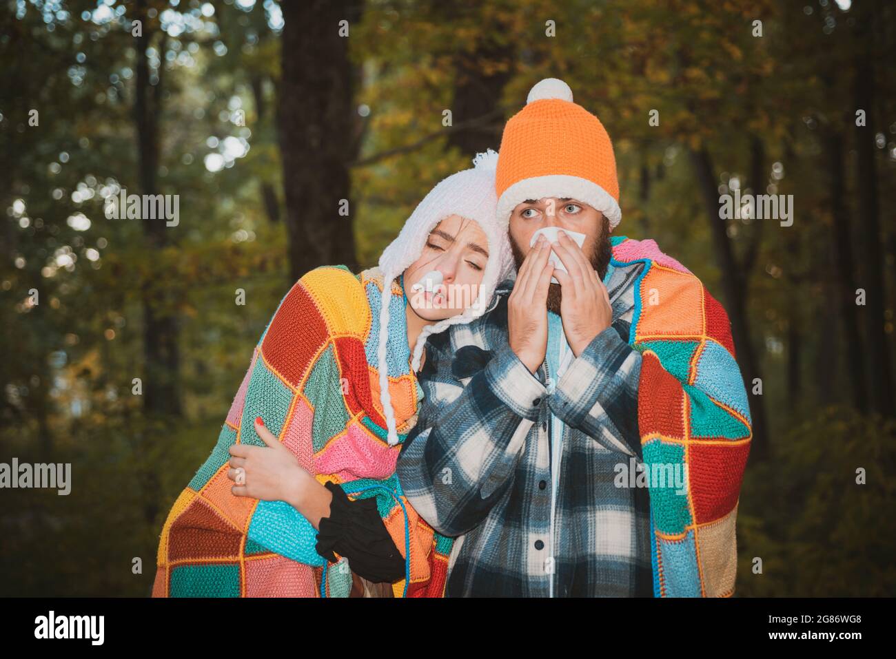 Showing sick couple sneezing at autumn park. Girl with handkerchief and ...