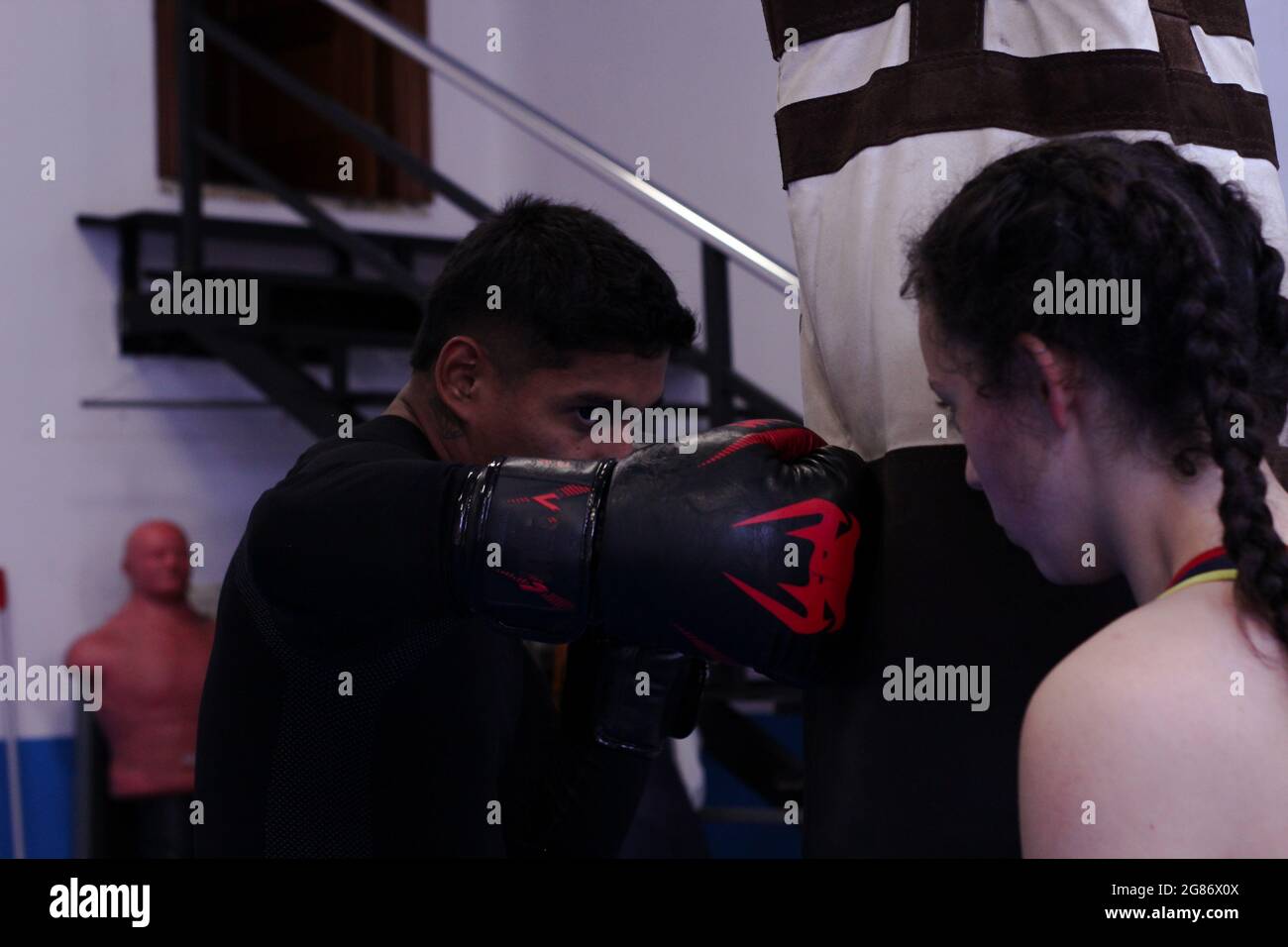 Young Spanish female coach holding punching bag to professional Latin ...