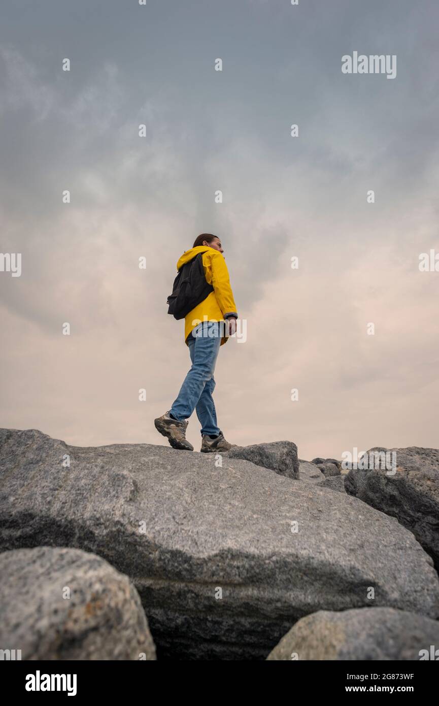 rear view of a woman backpacker wearing a yellow jacket walking over ...