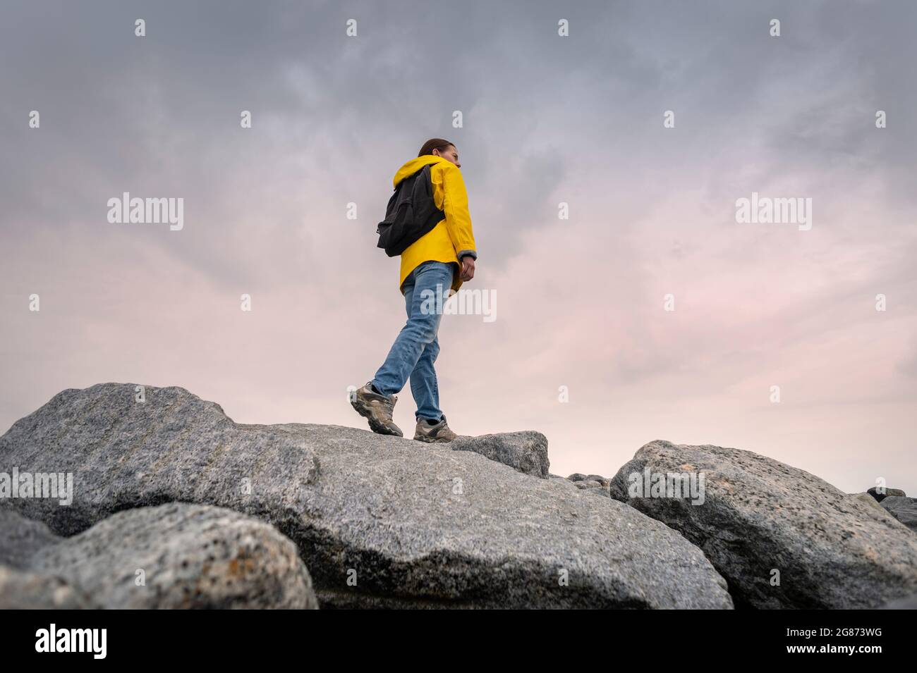 rear view of a woman backpacker wearing a yellow jacket walking over ...