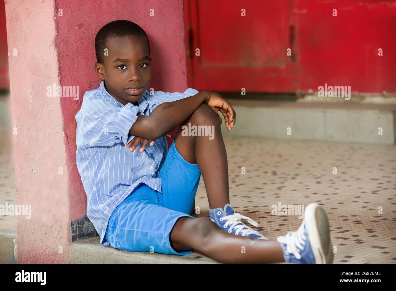 Happy boy sitting alone on the outside against a wall painted in red ...