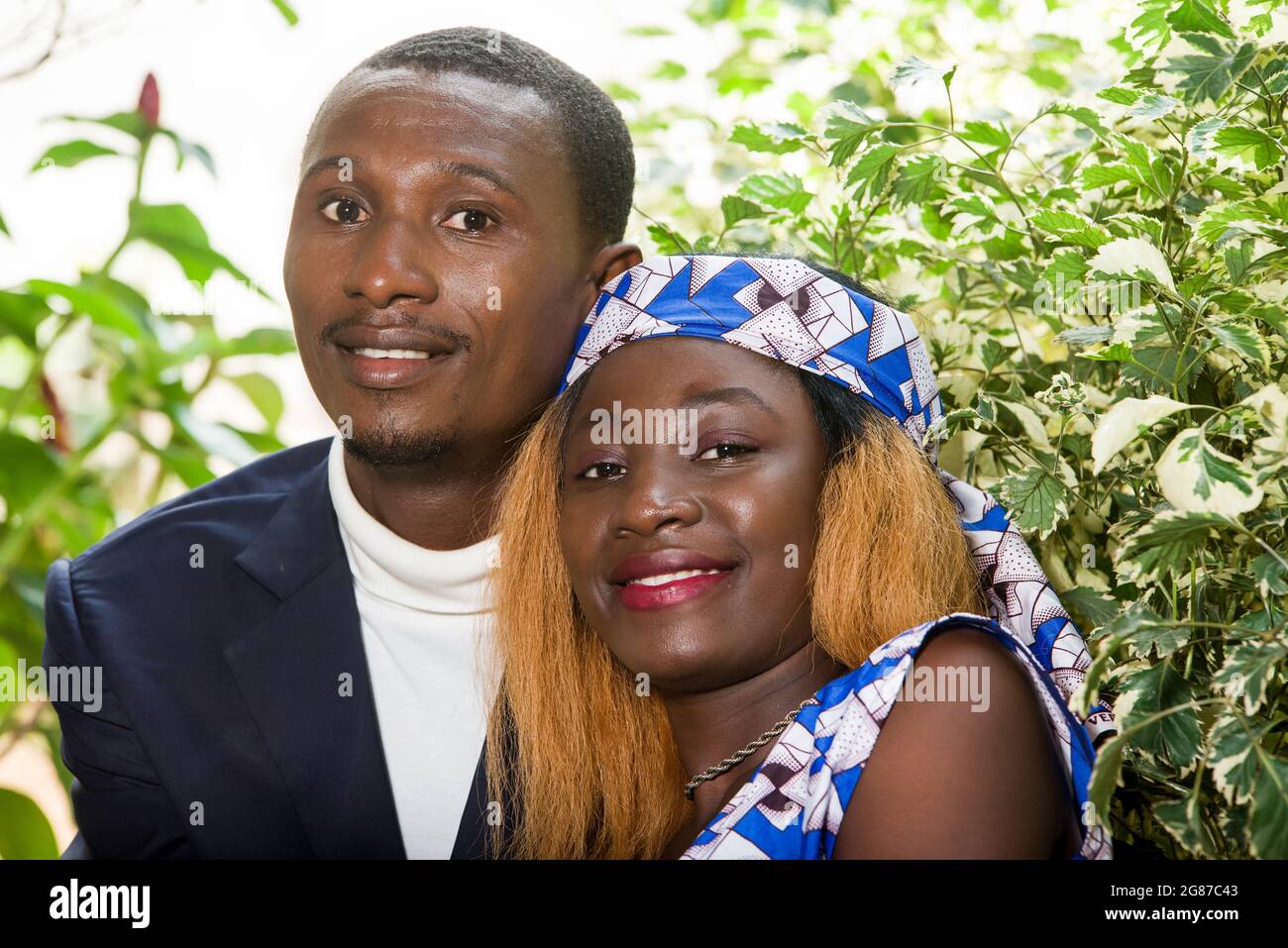 young african couple sitting in an embracing park looking at the camera ...