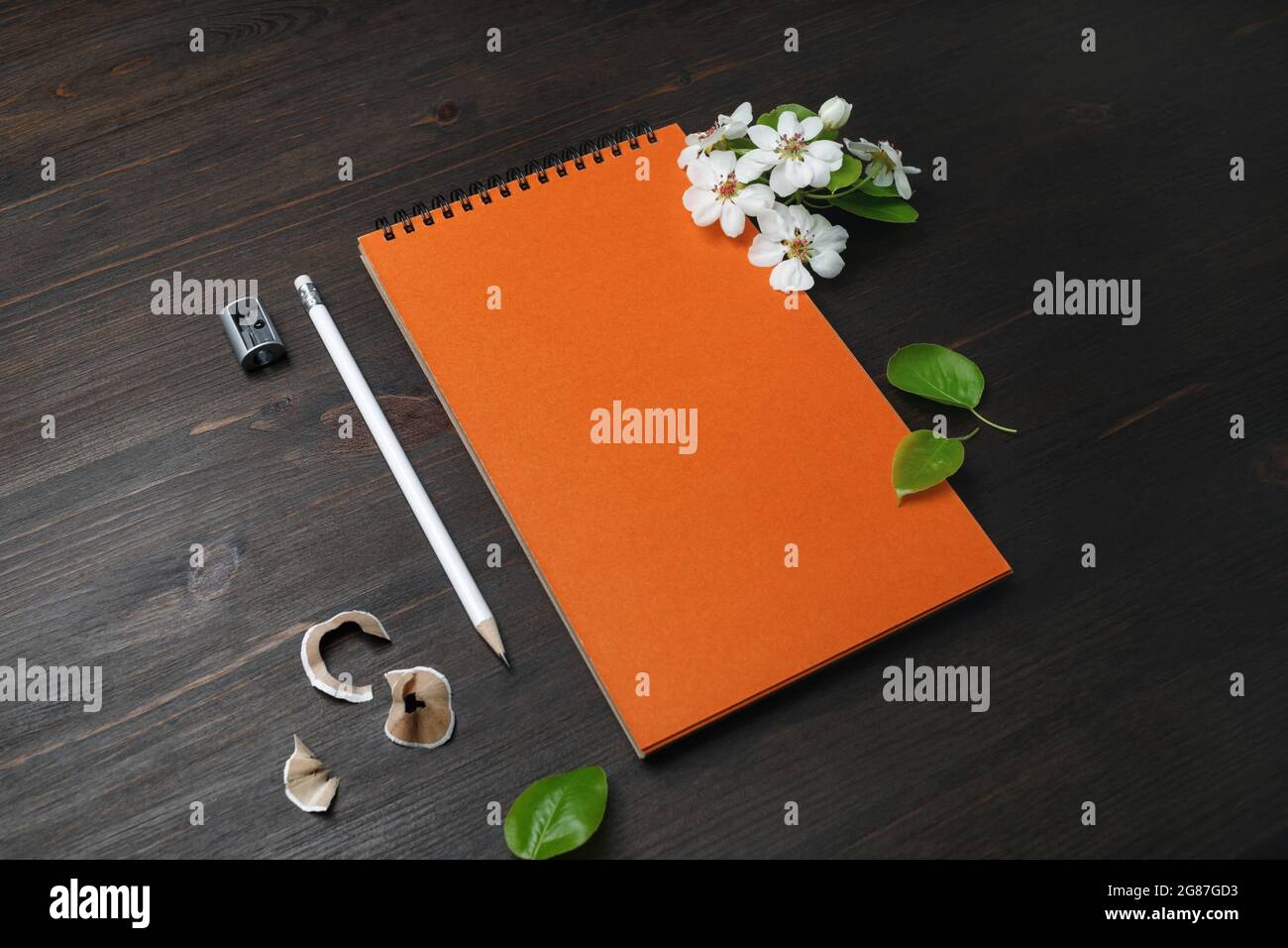 Blank orange notebook, pencil, sharpener and flowers on wooden ...