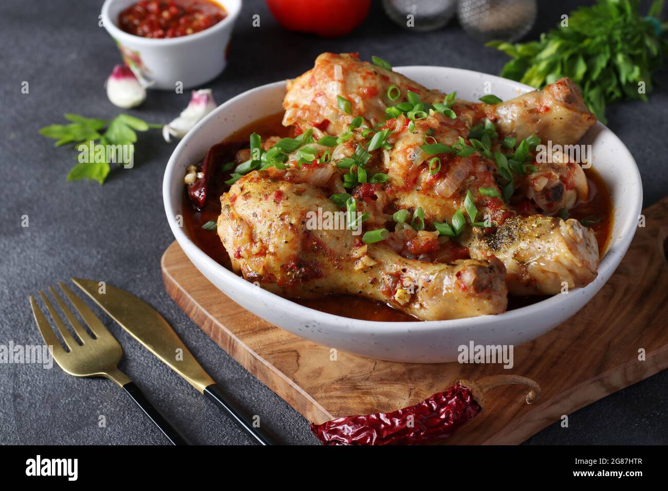 Georgian meat dish chashushuli with chicken and tomato on wooden board on dark gray table. Close ...