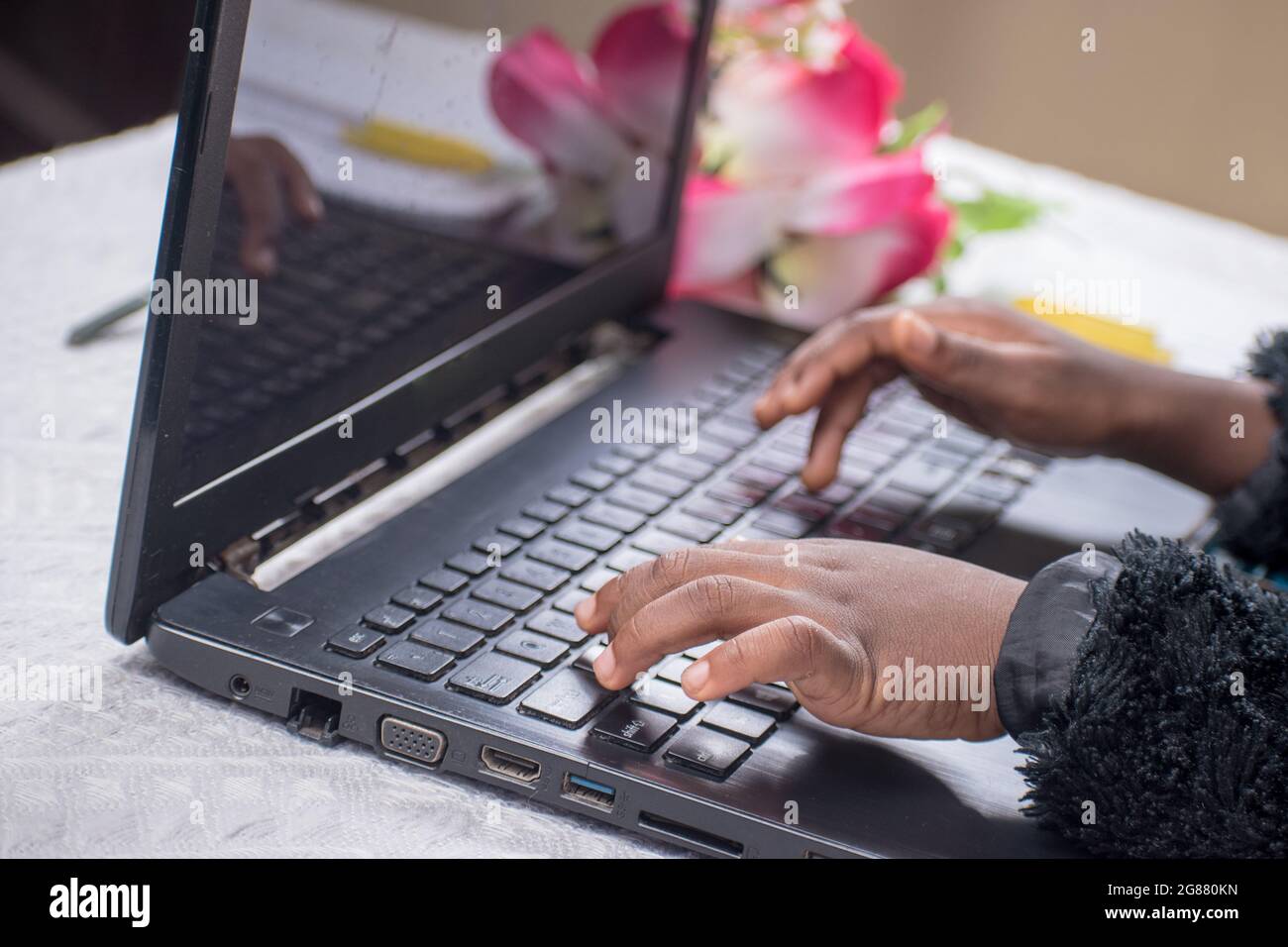 Hands of an African female or girl child typing on a black laptop's ...
