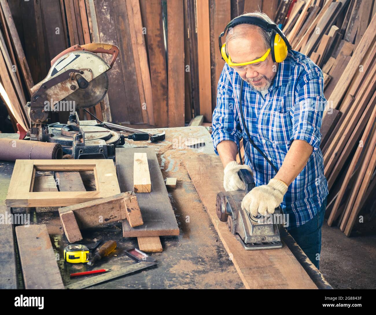 Happy senior carpenter using an electric planer with a wooden plank in ...