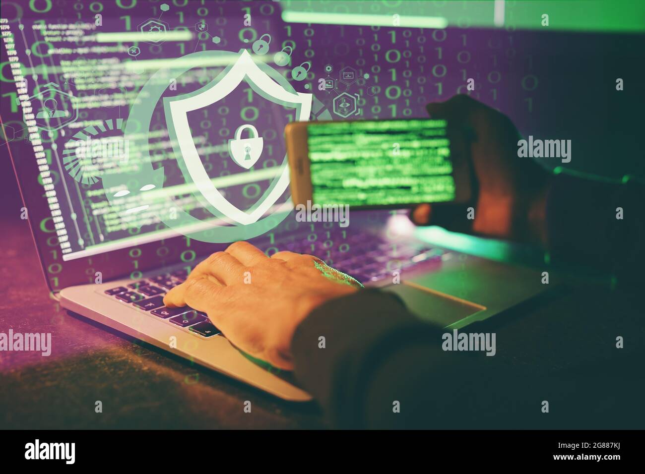 Hacker with mobile phone using computer in dark room Stock Photo - Alamy