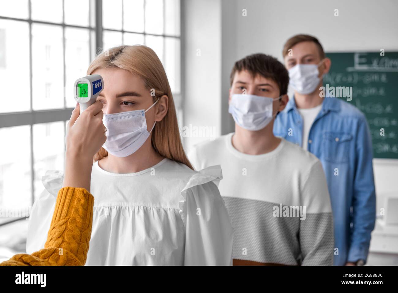Teacher measuring student's temperature in classroom before exam Stock ...