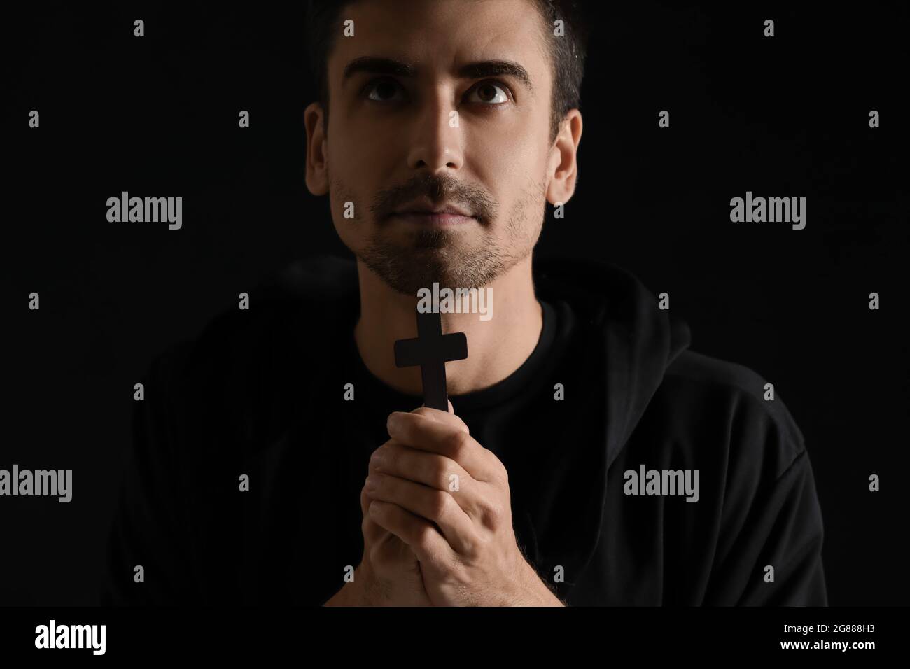 Religious young man with cross praying on dark background Stock Photo ...