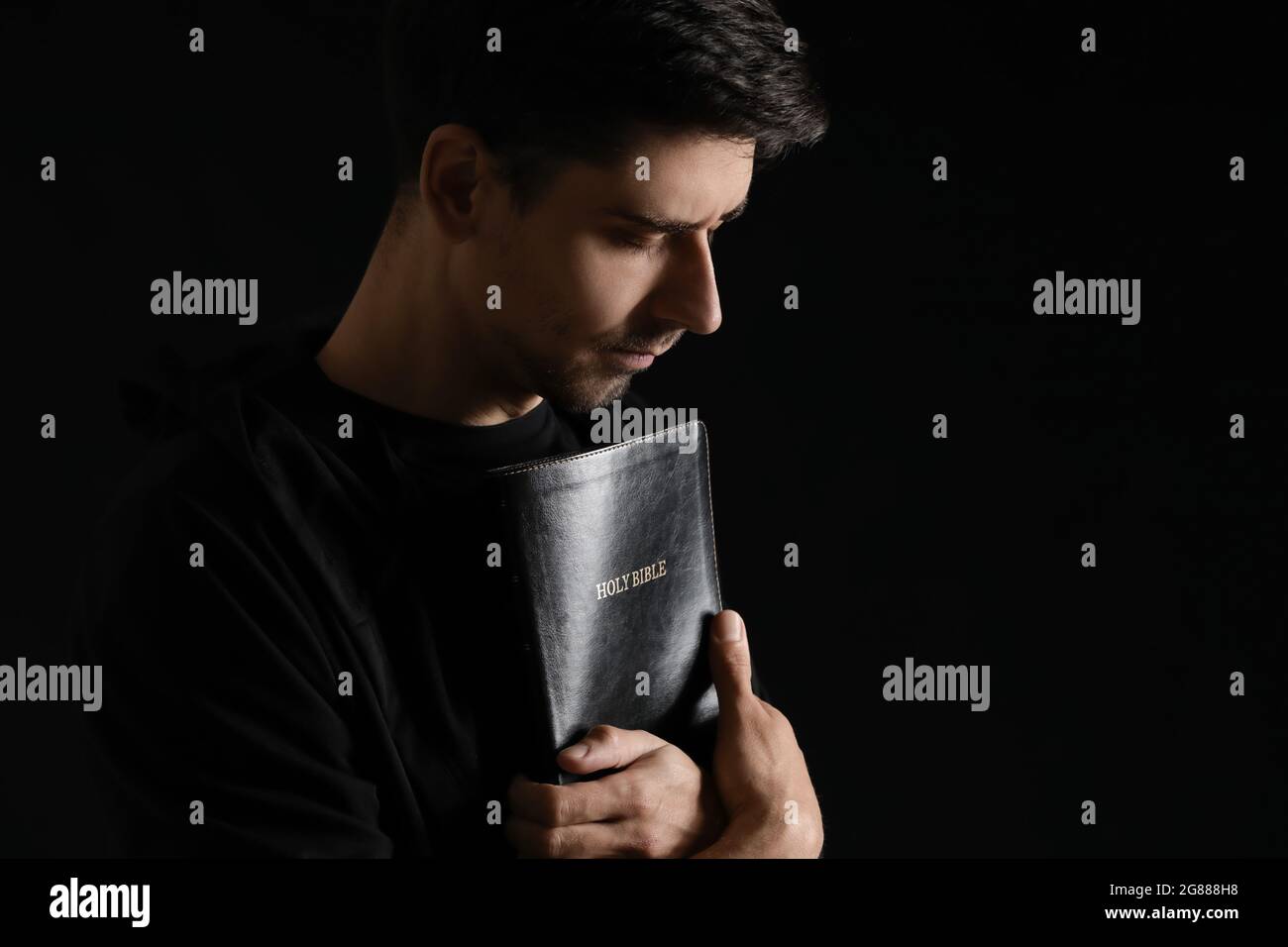 Religious young man with Bible praying on dark background Stock Photo ...