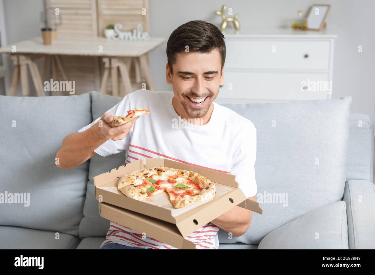 Young man eating tasty pizza at home Stock Photo - Alamy