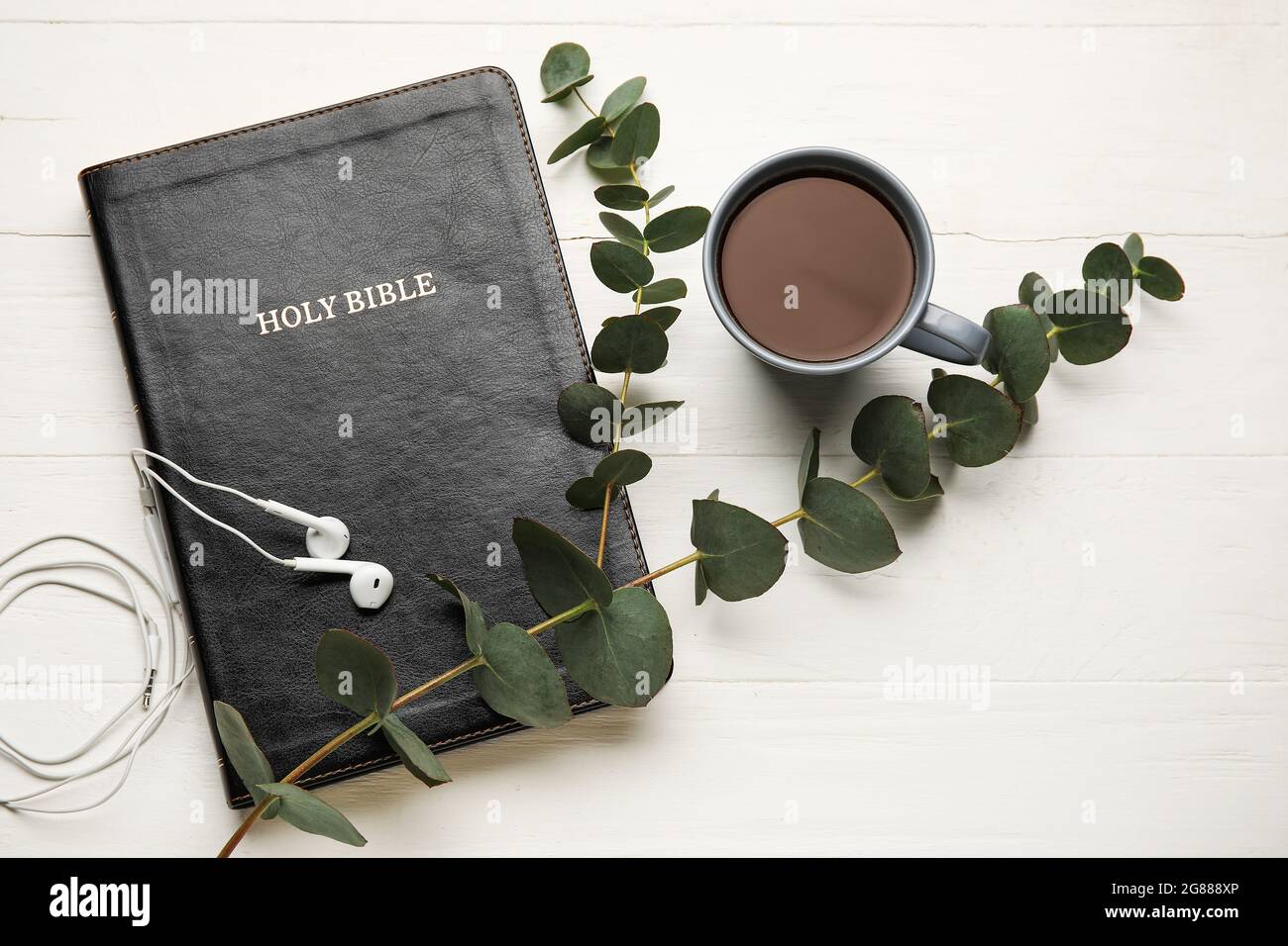 Holy Bible, cup of coffee, earphones and eucalyptus branch on light ...