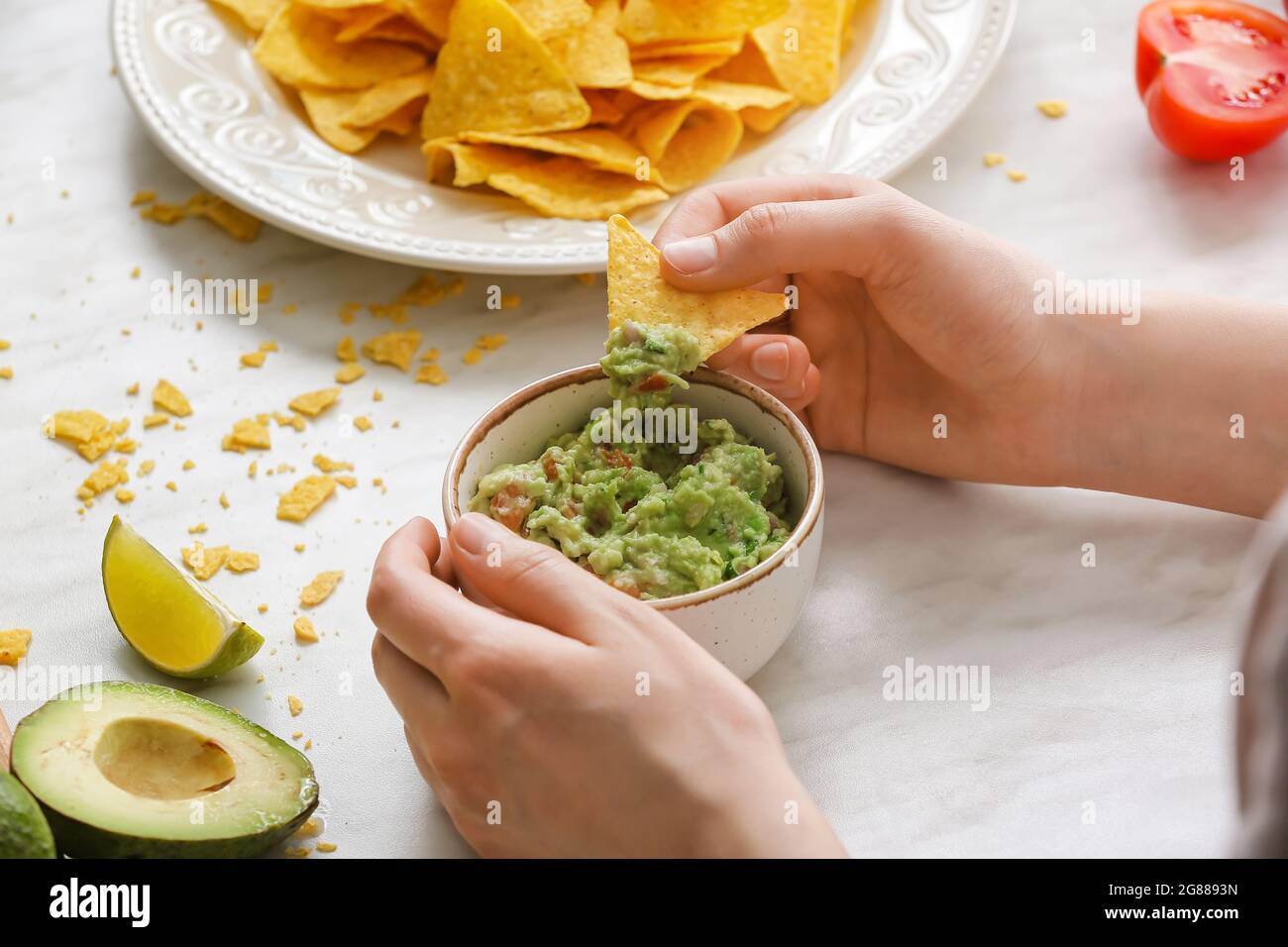 Woman eating tasty guacamole with nachos on light table, closeup Stock ...