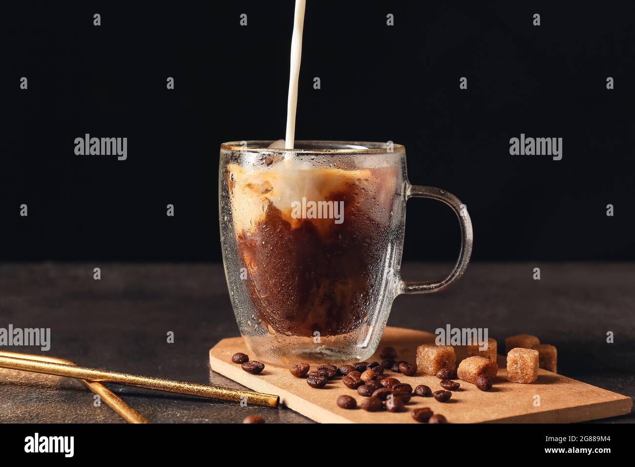 Pouring milk into cup with cold coffee on dark background Stock Photo ...