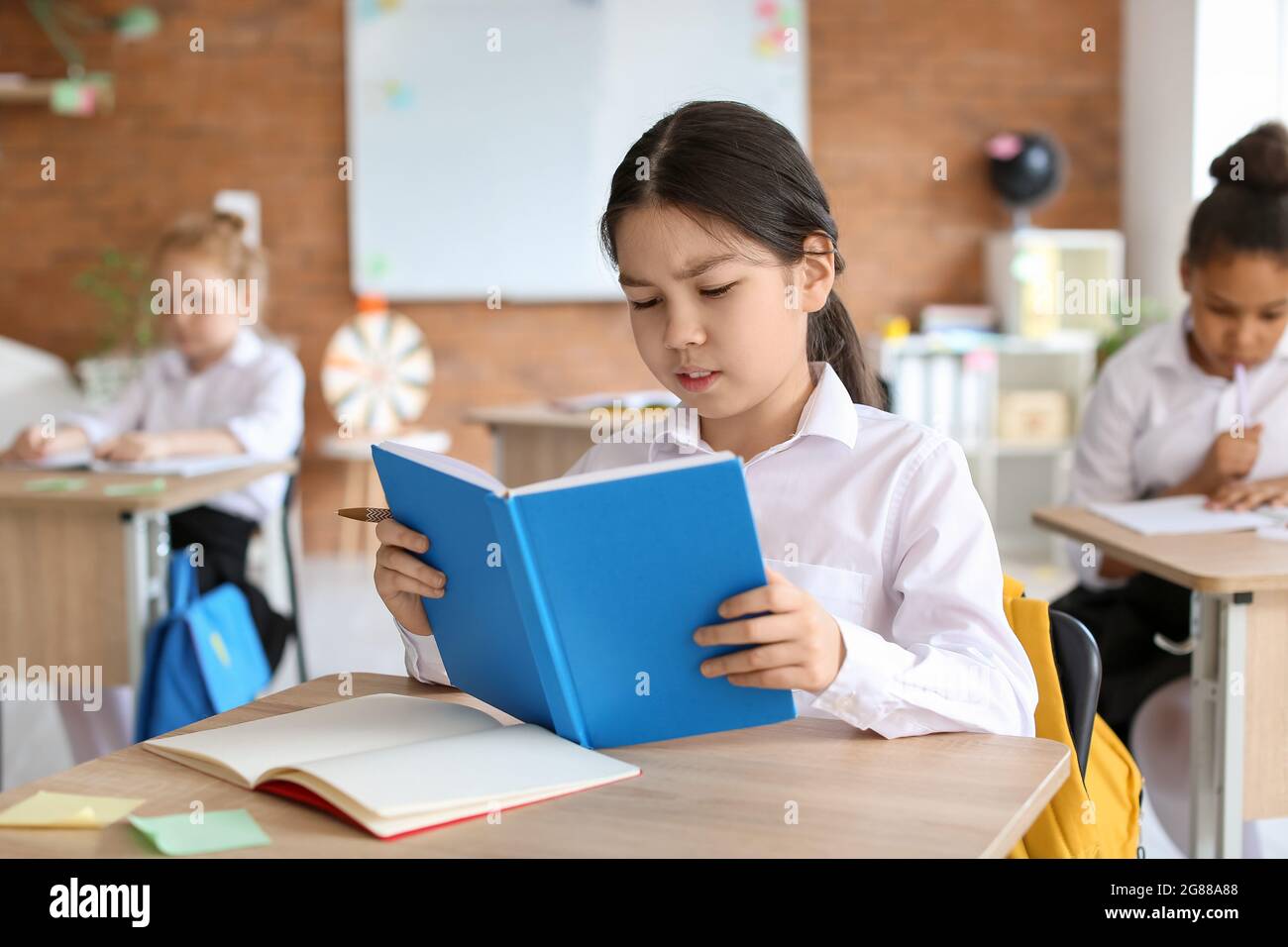 Cute little girl reading book during lesson at school Stock Photo - Alamy